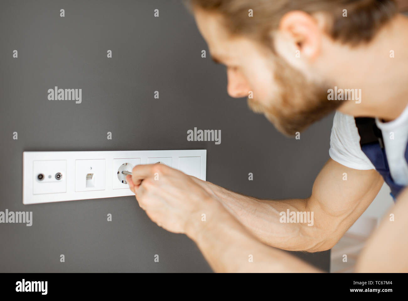 Electrician mounting electric sockets on the grey wall at home Stock ...