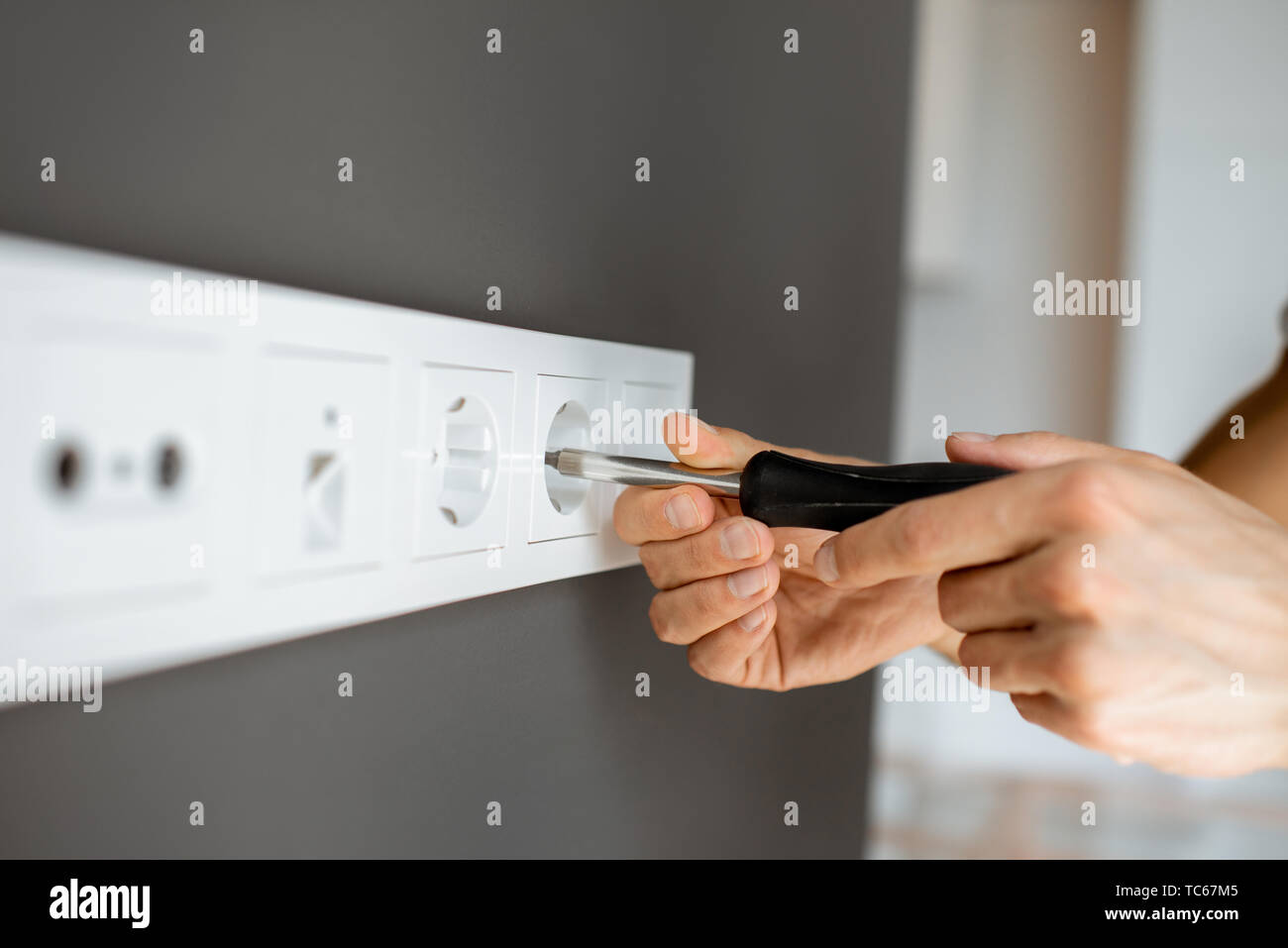 Electrician mounting electric sockets on the grey wall at home Stock ...