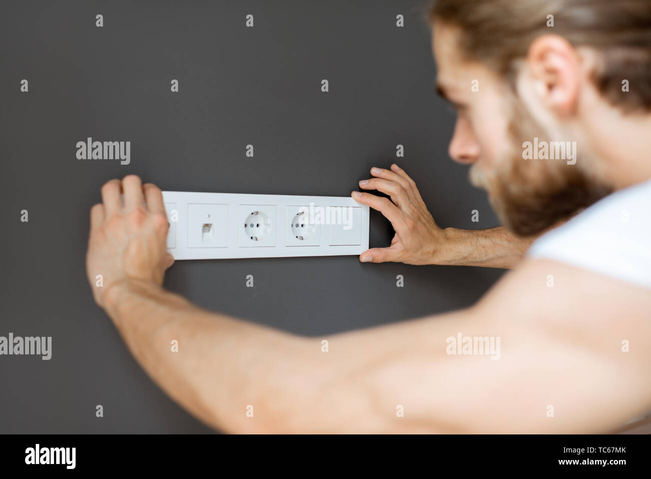 Electrician mounting electric sockets on the grey wall at home Stock ...