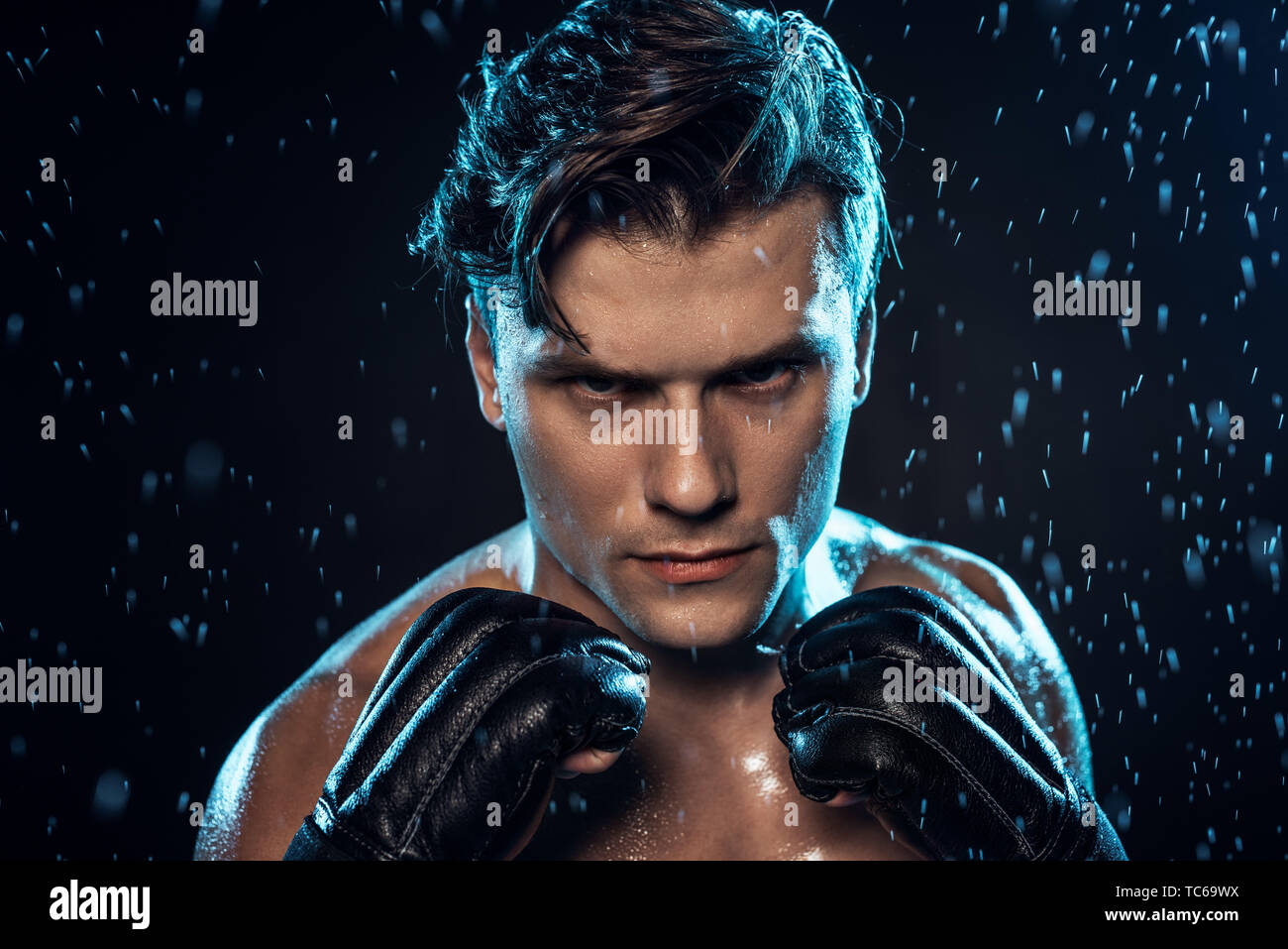 Front view of boxer in leather gloves standing under water drops on ...
