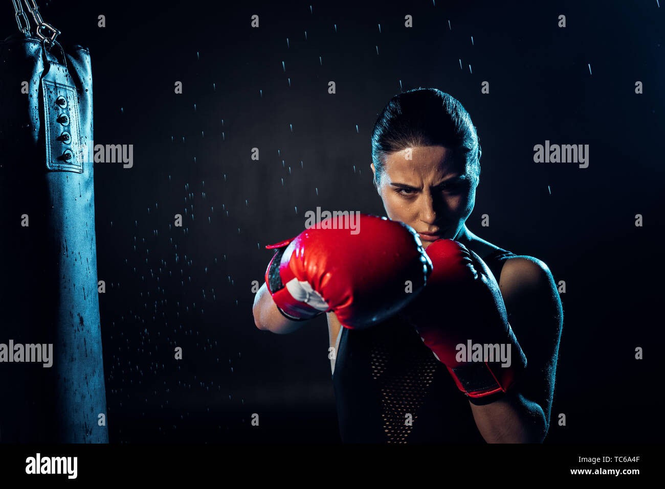 Concentrated boxer in red boxing gloves standing under water drops on ...