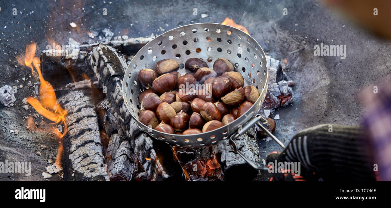 Panorama banner of a man roasting fresh chestnuts in a metal roaster ...