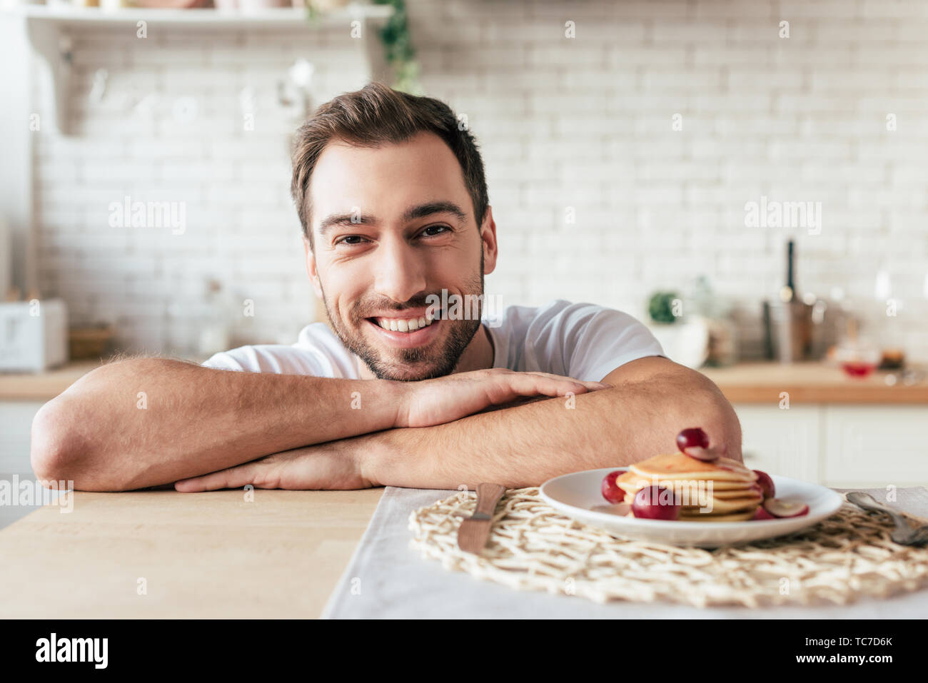 front view of laughing man sitting at table with plate on pancakes ...