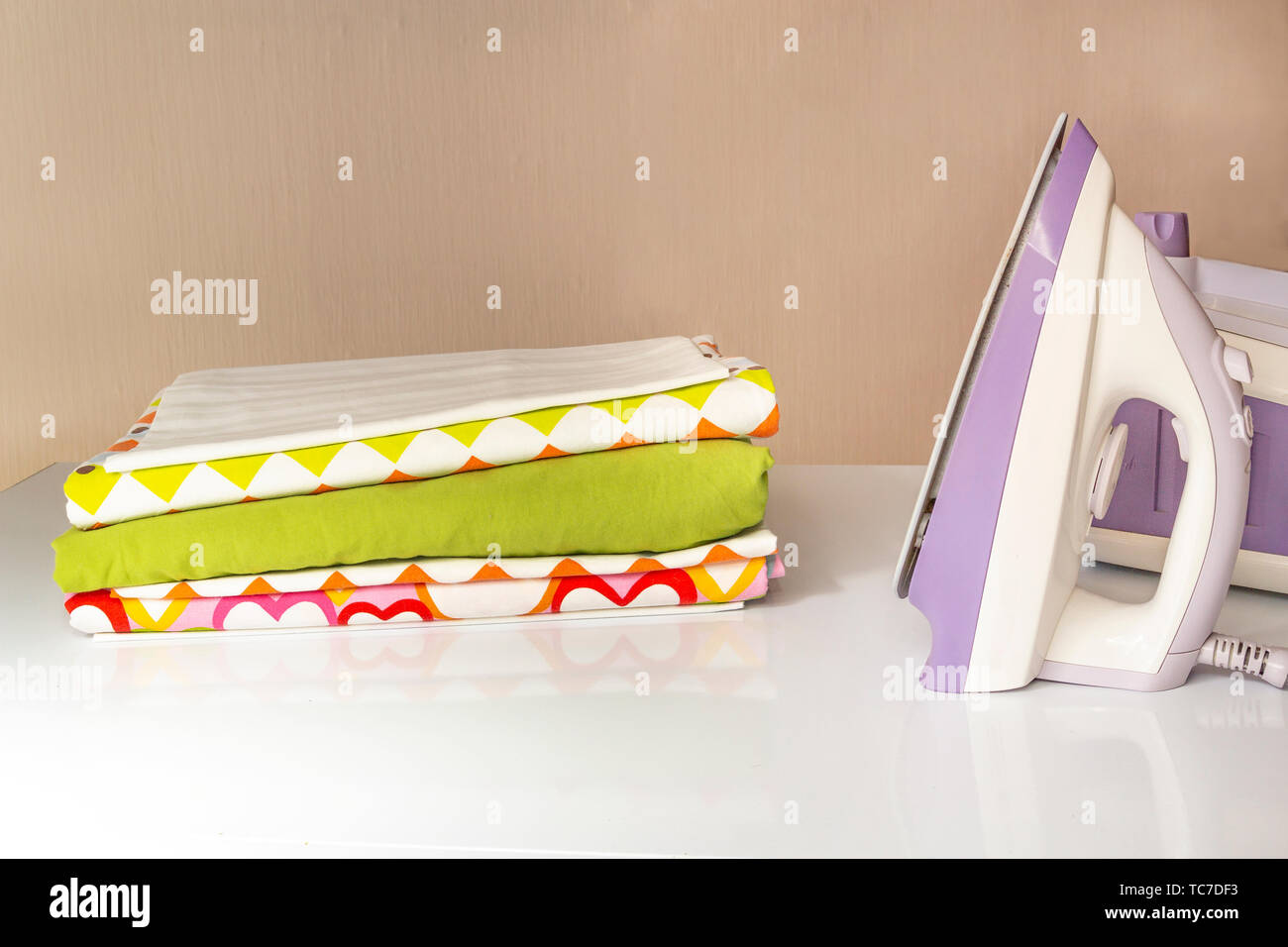 Iron and a stack of ironed linen lying on a white table Stock Photo - Alamy