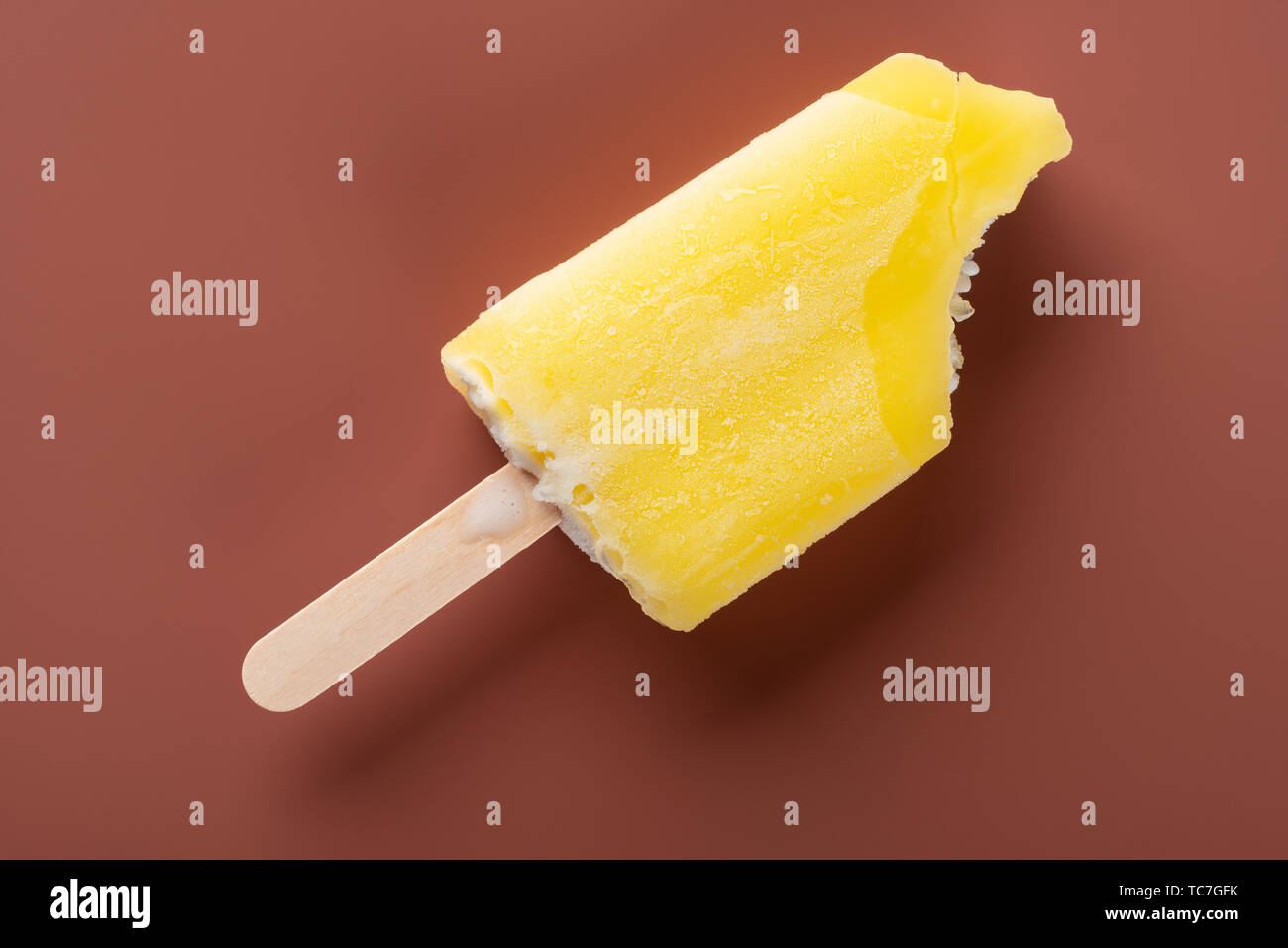 yellow popsicle with bites on a brown background Stock Photo - Alamy