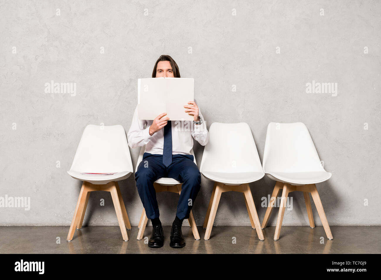 man in formal wear covering face with blank paper while sitting on ...