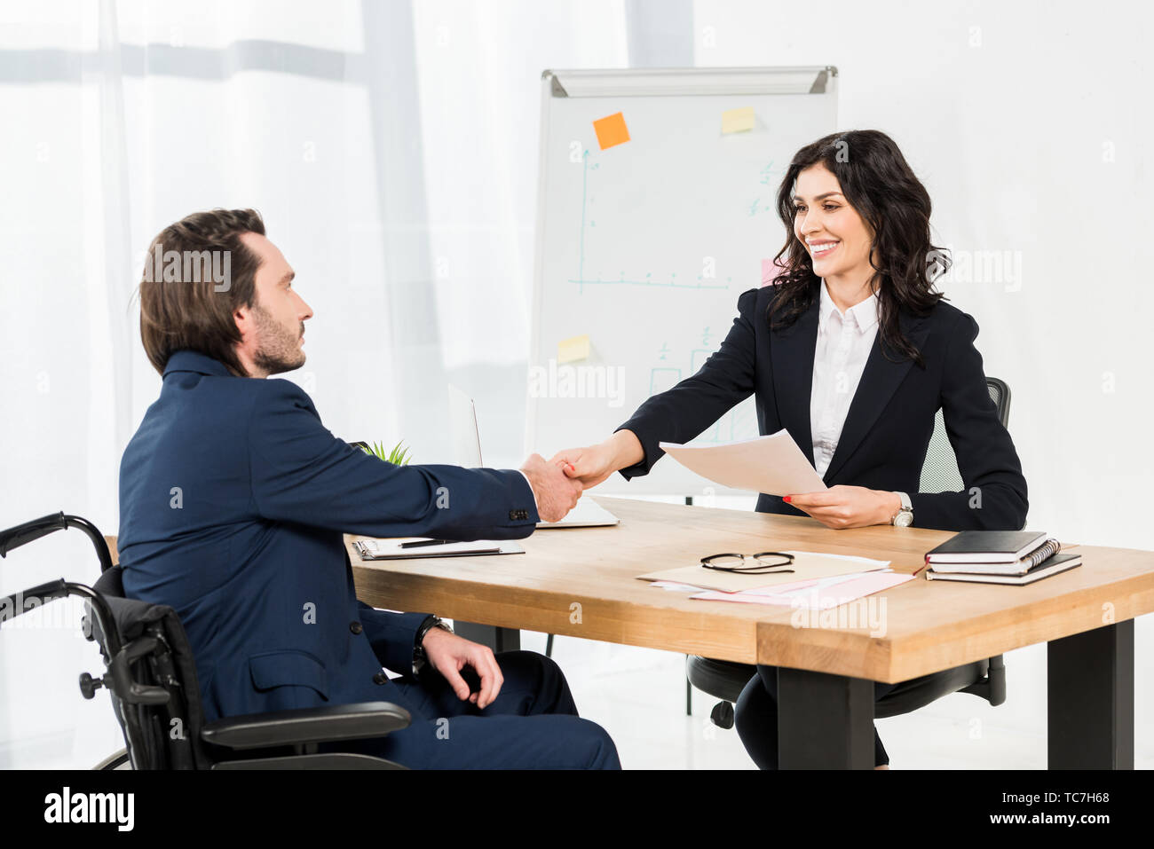 happy recruiter shaking hands with disabled man while holding documents ...