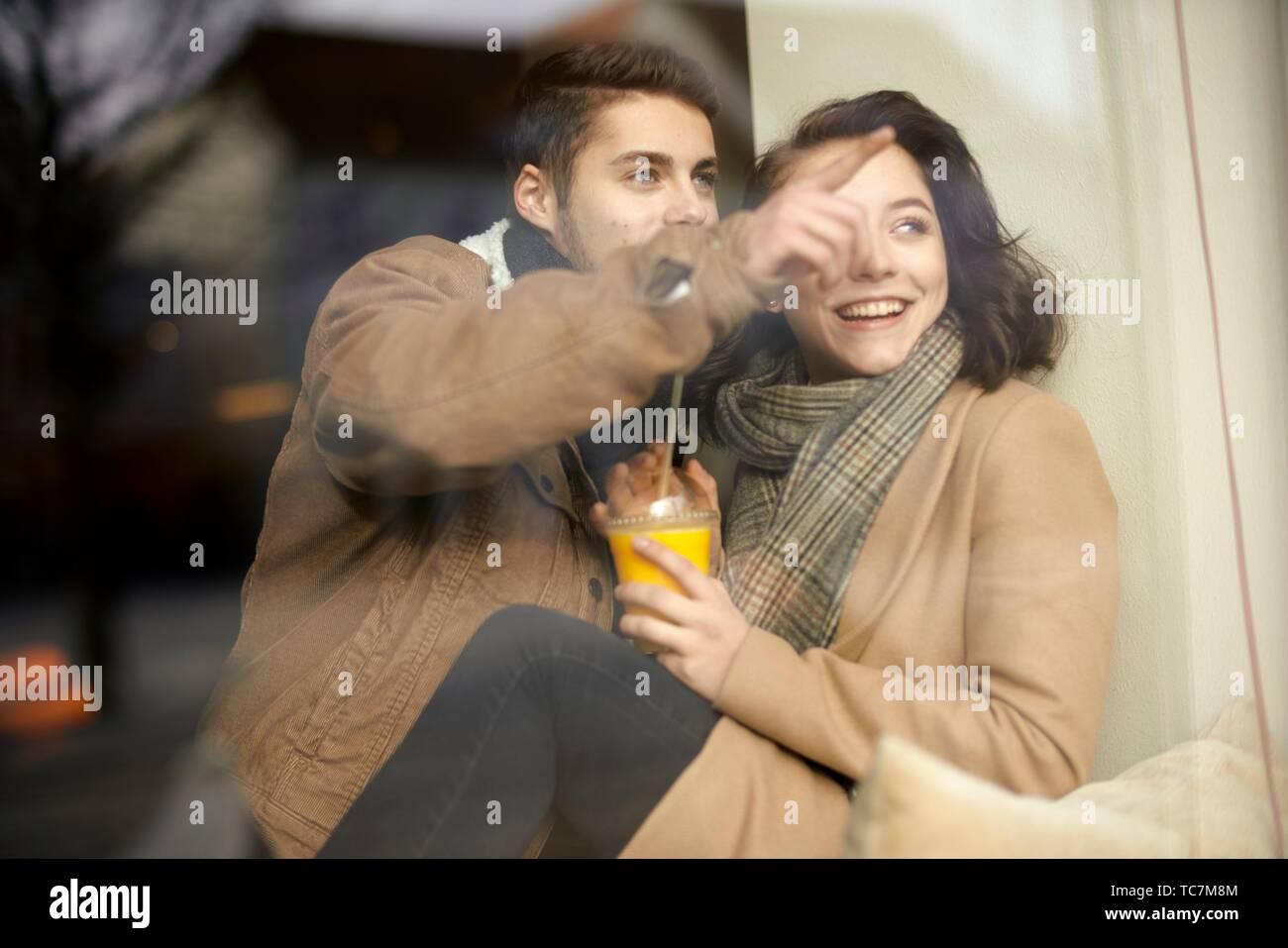 man pointing out of window, showing girlfriend something, behind window ...