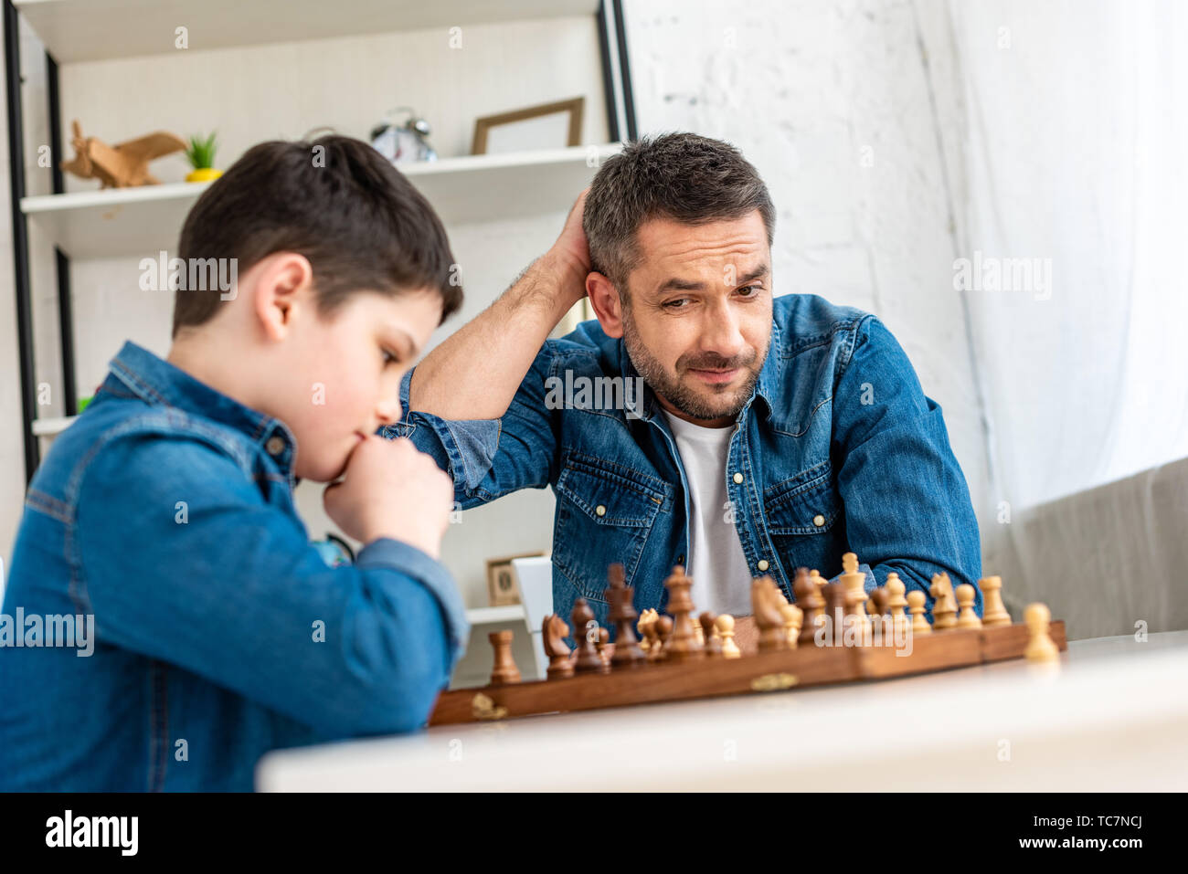 selective focus of father and son in denim playing chess at home Stock ...