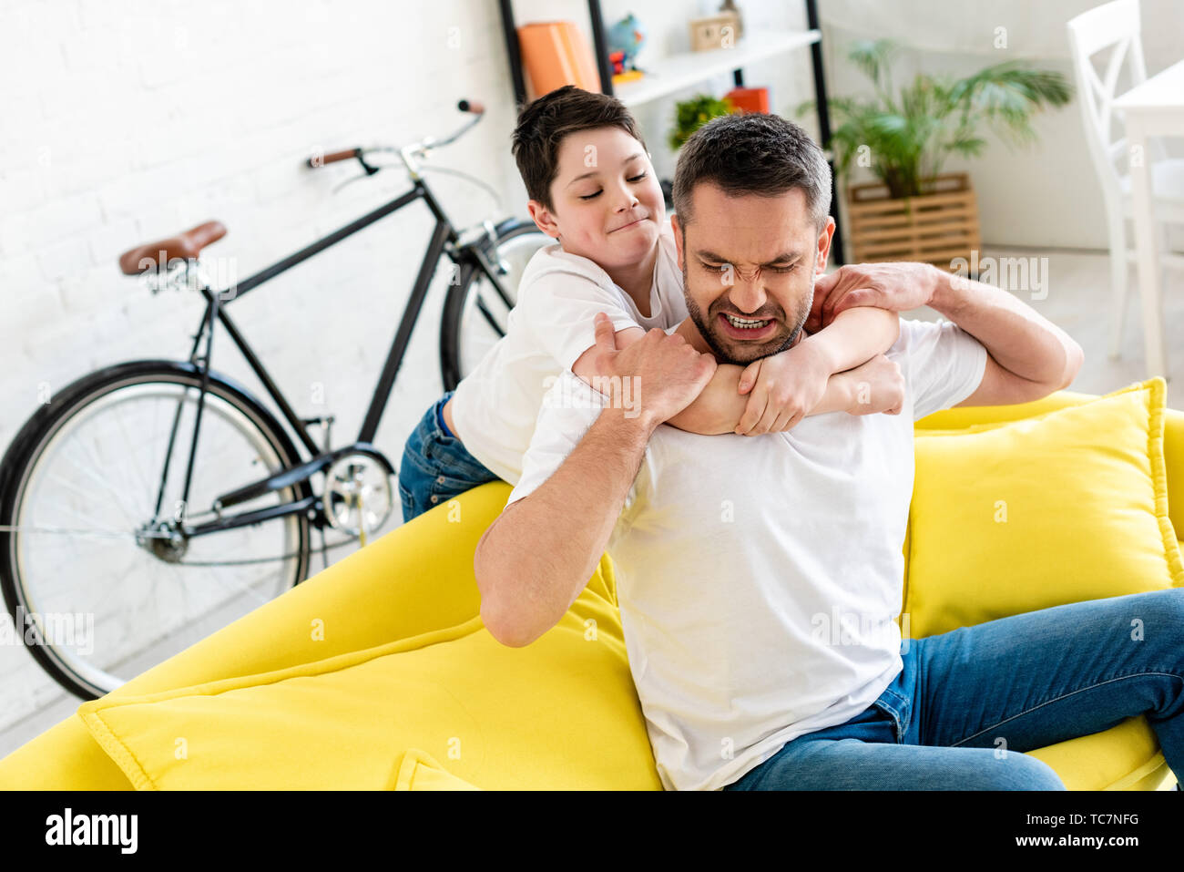 son hugging irritated father sitting on couch at home Stock Photo - Alamy