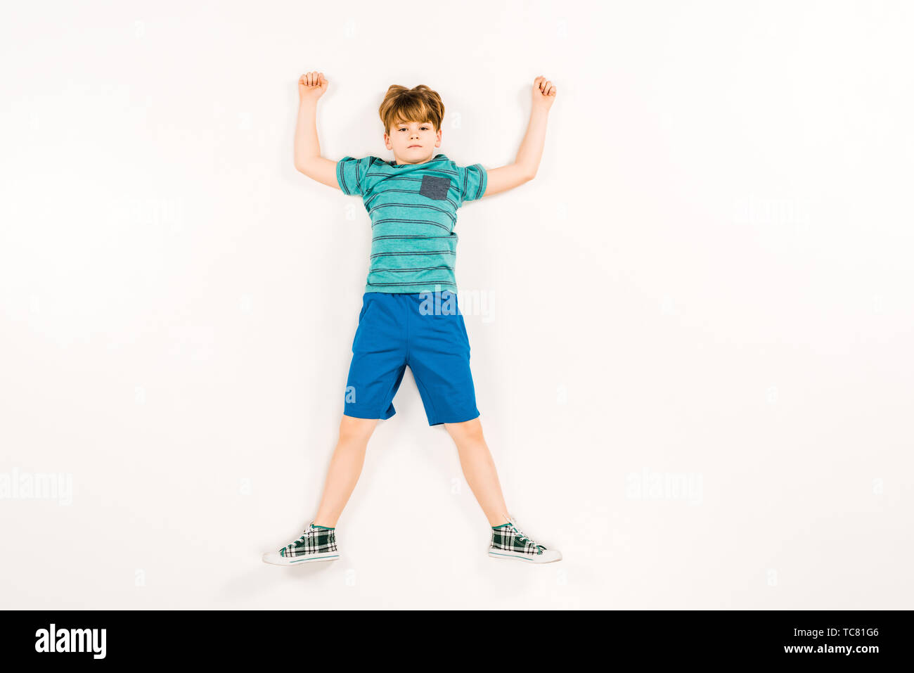 top view of cute kid with hands above head looking at camera on white ...