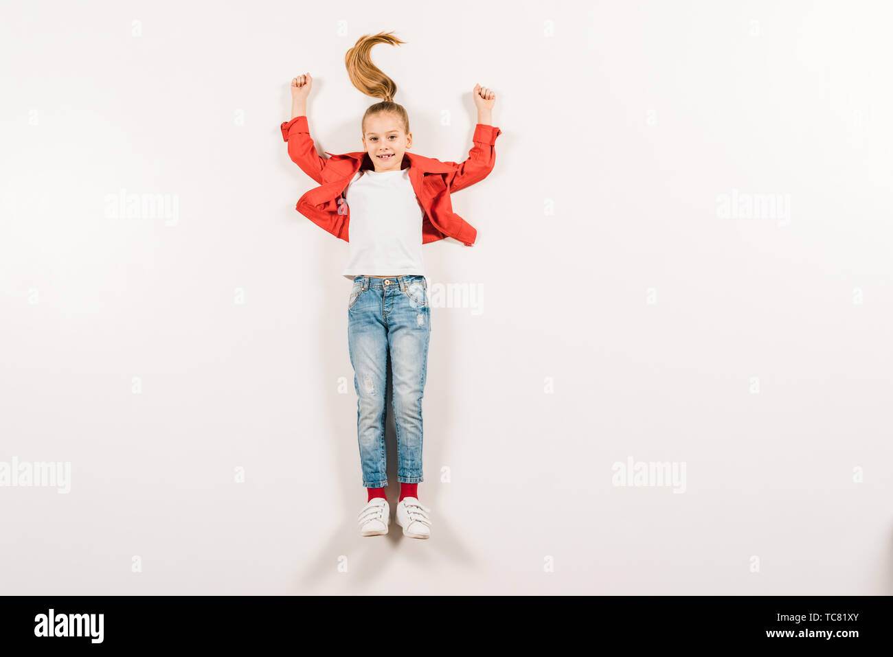 top view of happy kid with hands above head lying on white Stock Photo ...