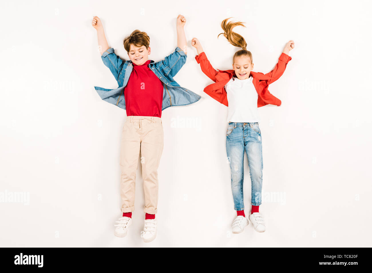 top view of cheerful kids with hands above head lying on white Stock ...