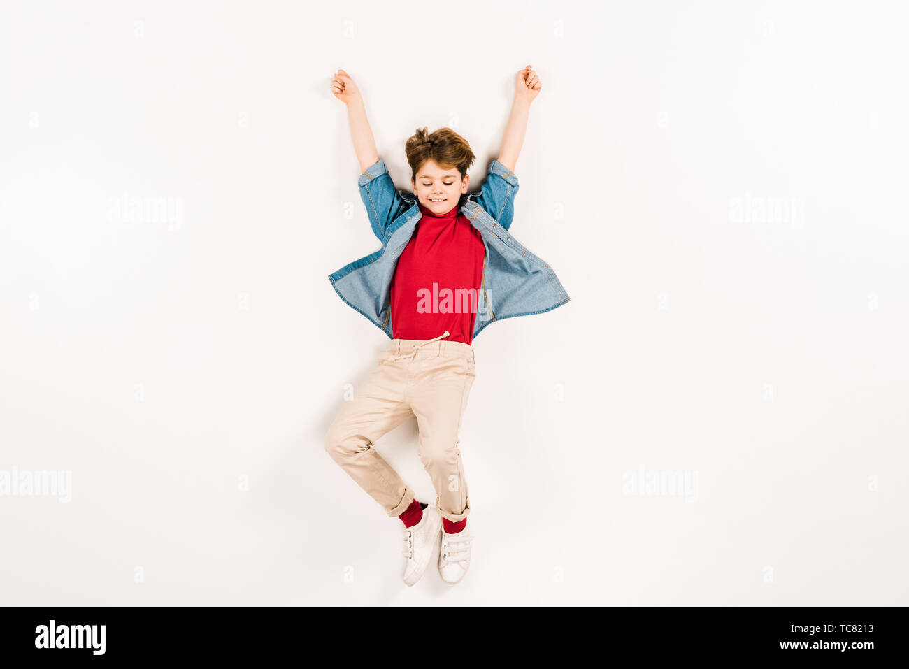 top view of cheerful kid with hands above head lying on white Stock ...