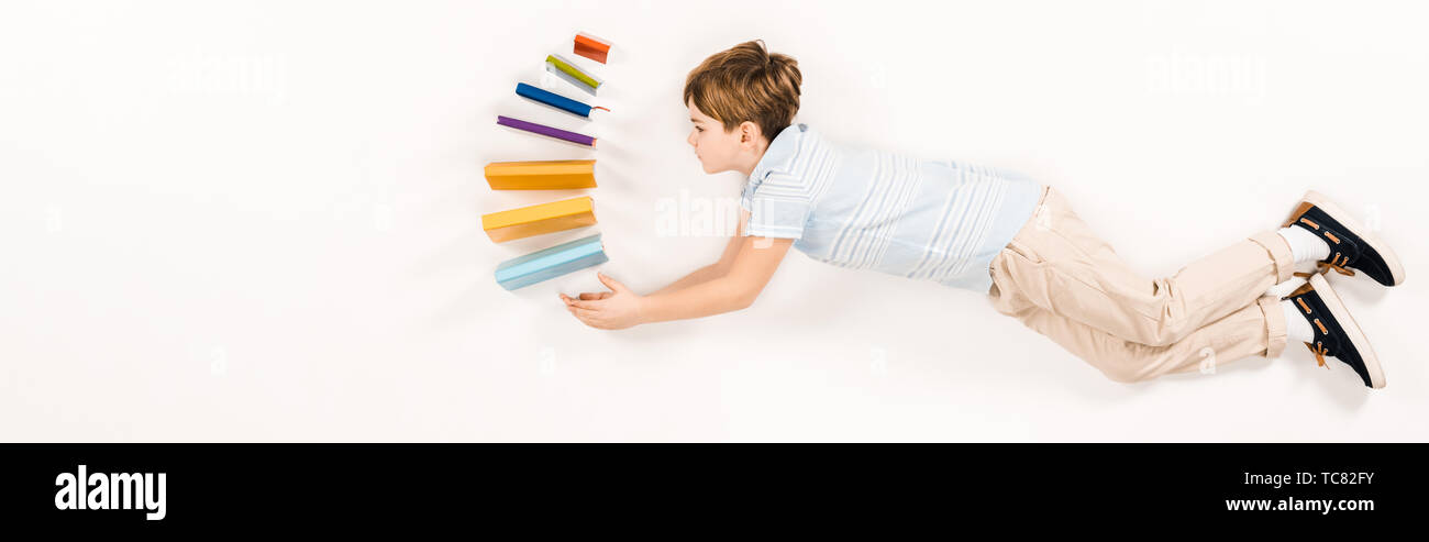 panoramic shot of cute kid holding colorful books while flying on white ...