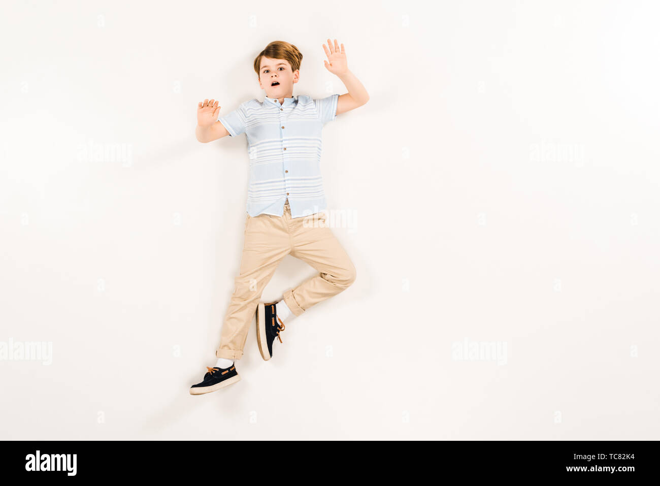 top view of scared kid gesturing while screaming and lying on white ...
