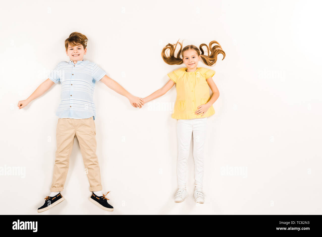 top view of cheerful kids holding hands and smiling on white Stock ...