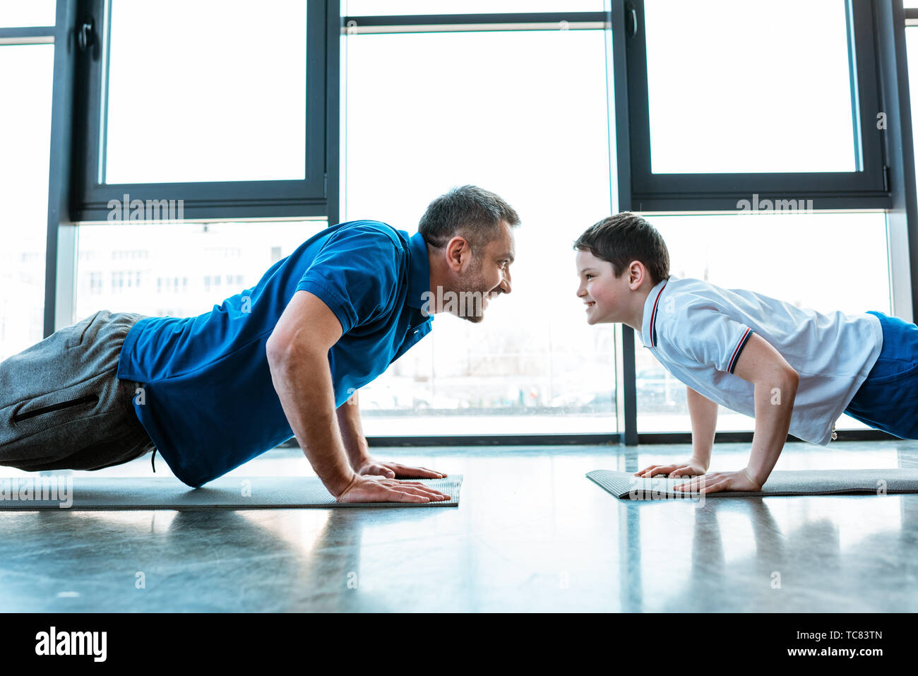 father and son looking at each other while doing push up exercise at ...