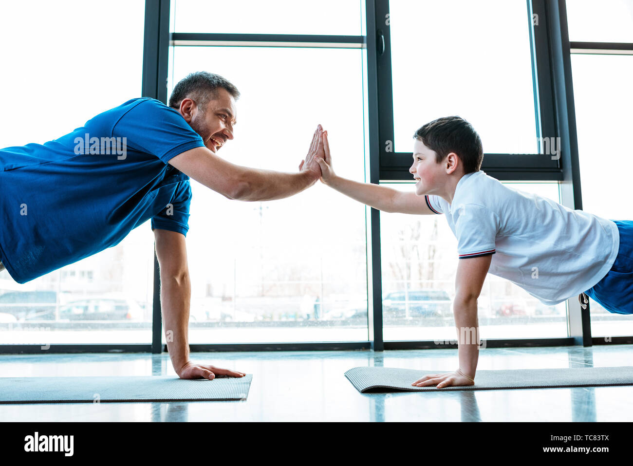 father and son doing high five sign while doing push up exercise at gym ...