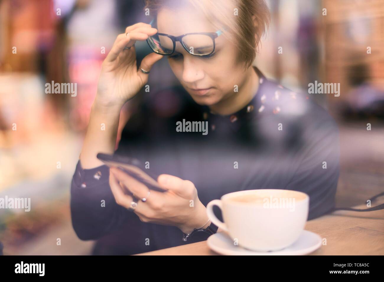 woman behind glass window touching glasses, using smartphone next to ...