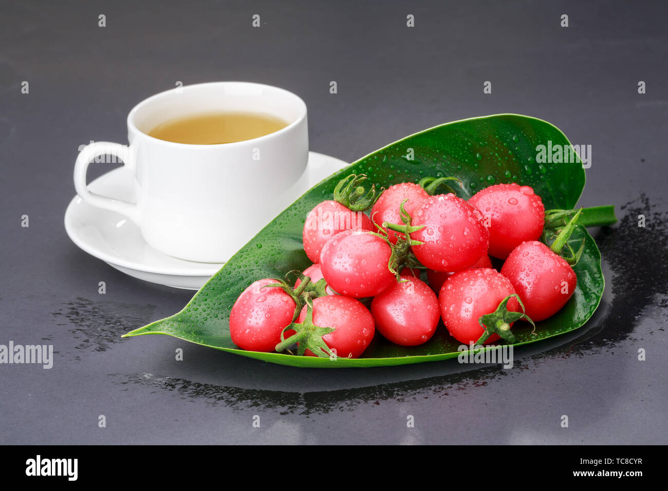 A bunch of little red tomatoes on green leaves on a black table top ...