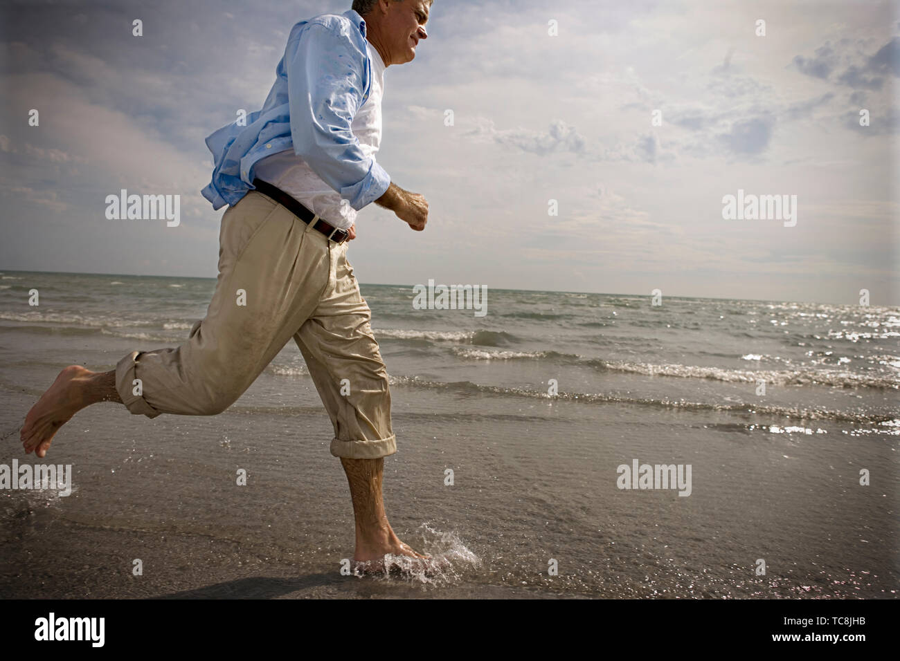 Mature man running through shallow water at the beach Stock Photo - Alamy
