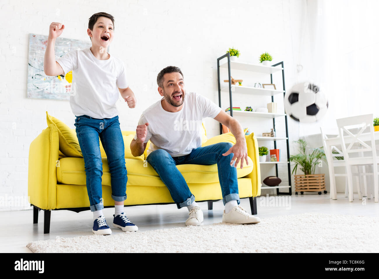 excited father and son cheering while watching sports match in Living ...