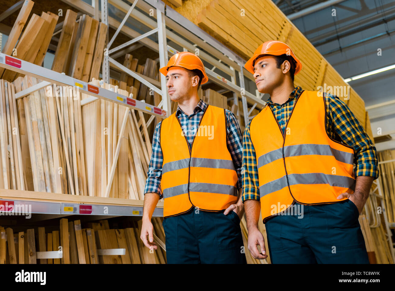 multicultural warehouse workers in safety vasts and helmets standing ...