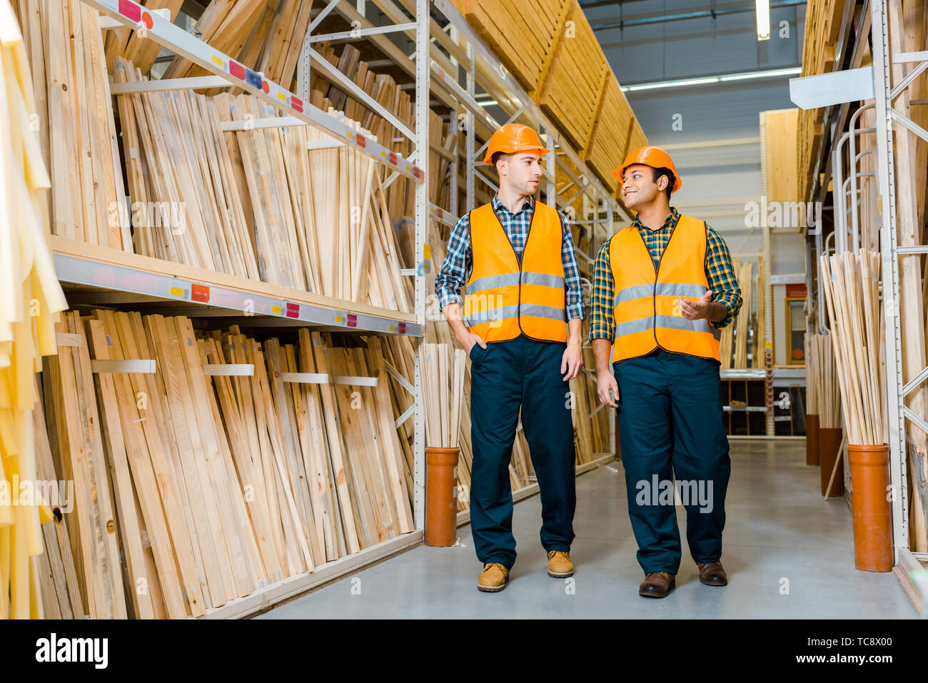 smiling multicultural workers talking while walking along racks with ...
