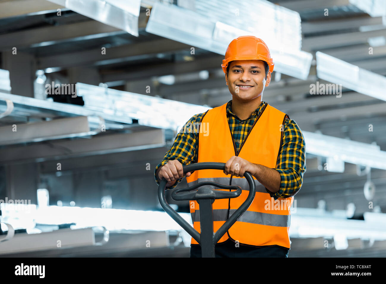 smiling indian warehouse worker standing near pallet jack, smiling and ...