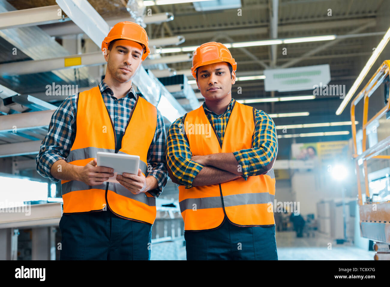 serious multicultural workers in safety vasts and helmets looking at ...
