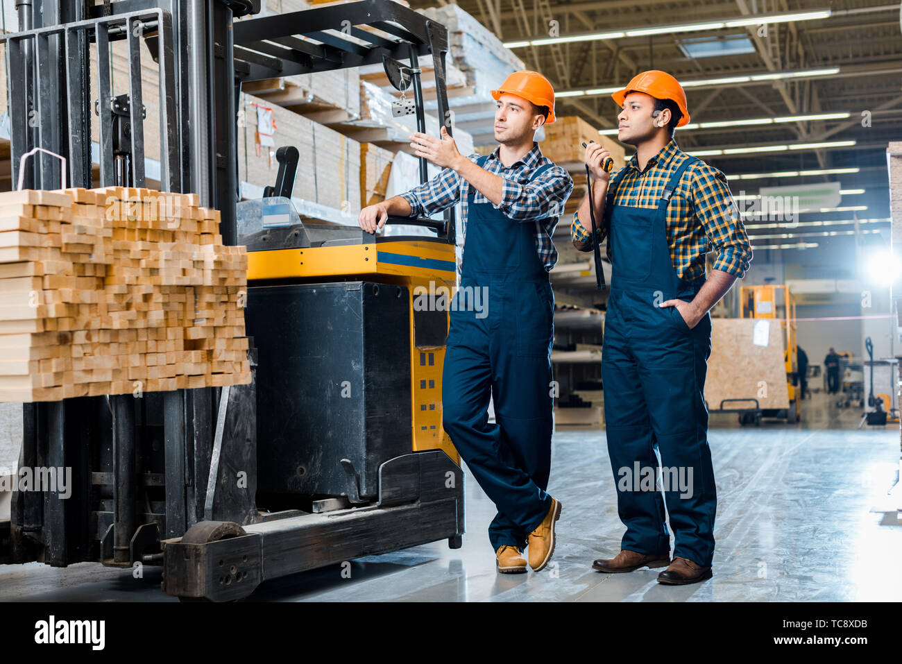 handsome multicultural warehouse workers in helmets standing near ...