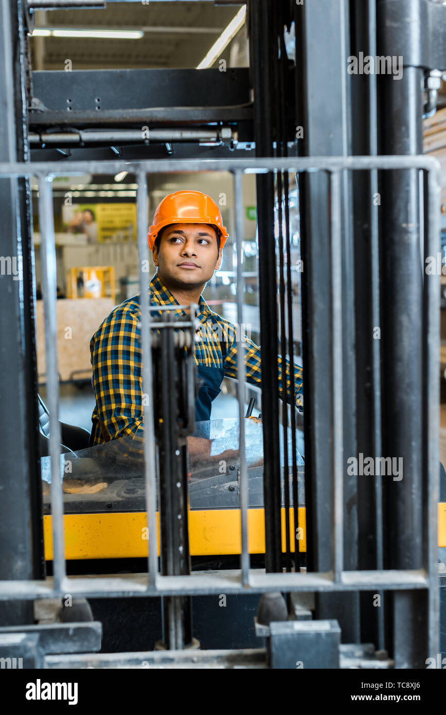 handsome, attentive indian worker sitting in forklift machine in ...