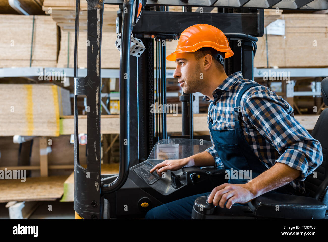 concentrated handsome worker in uniform and helmet operating forklift ...