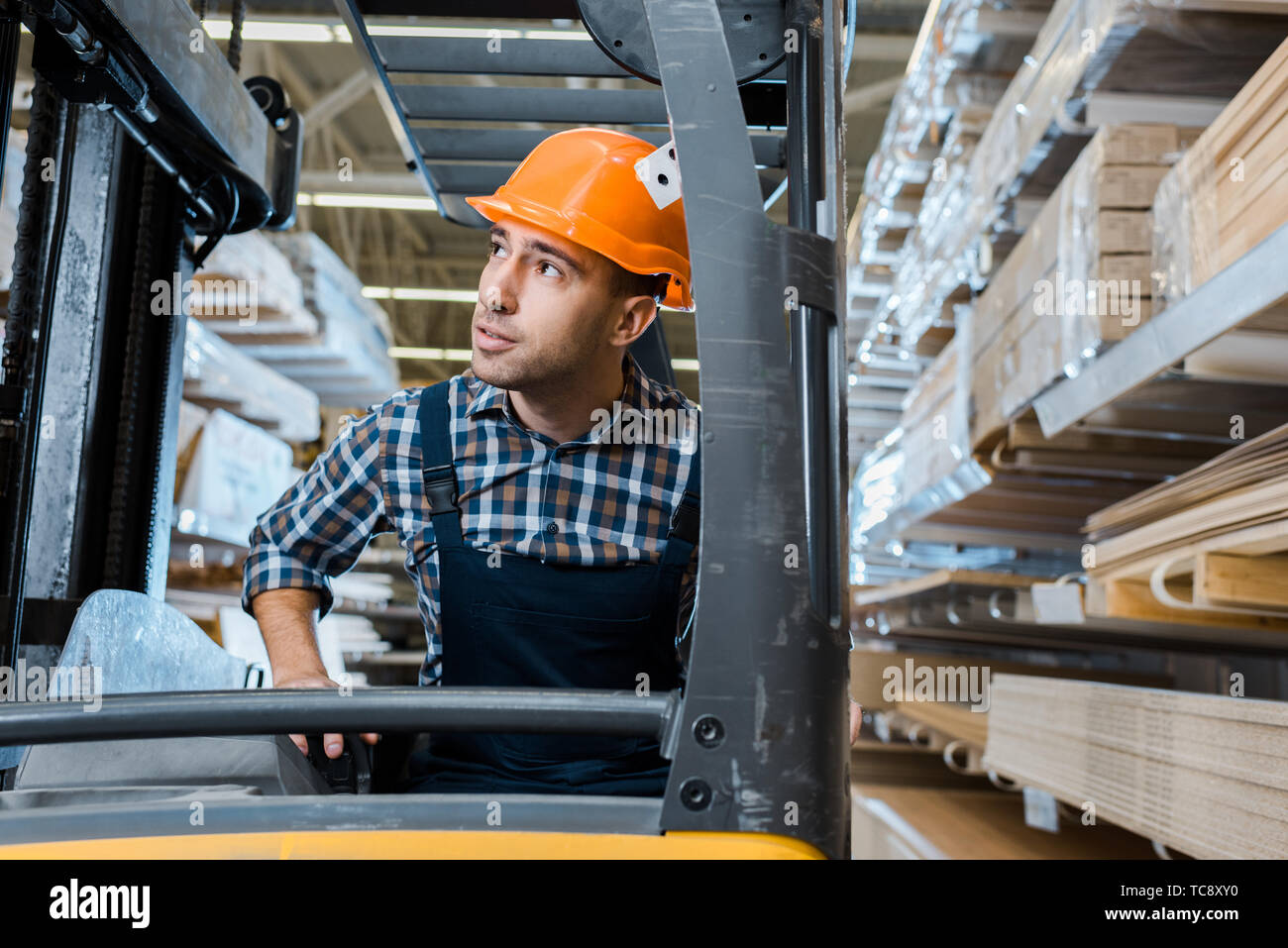 attentive warehouse worker in uniform and helmet operating forklift ...