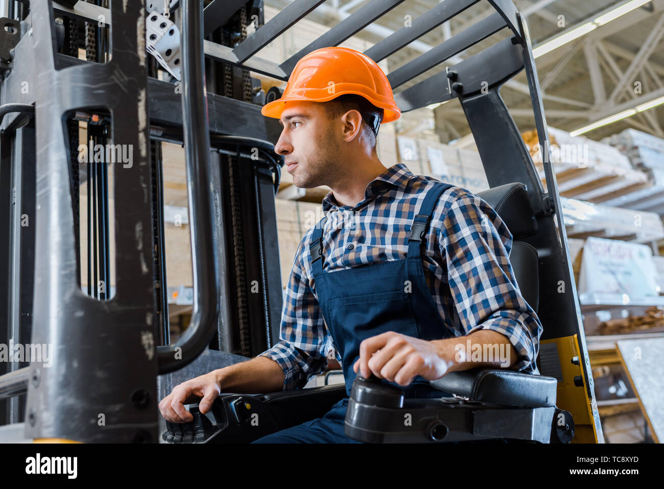 warehouse worker in uniform and helmet operating forklift machine Stock ...