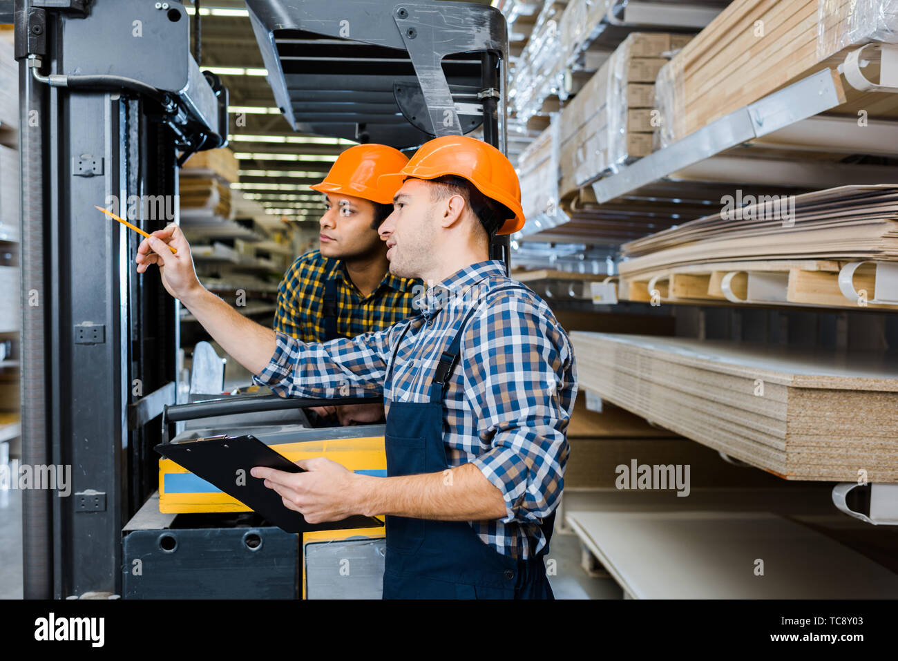 multicultural workers in uniform and plaid shirts working in warehouse ...