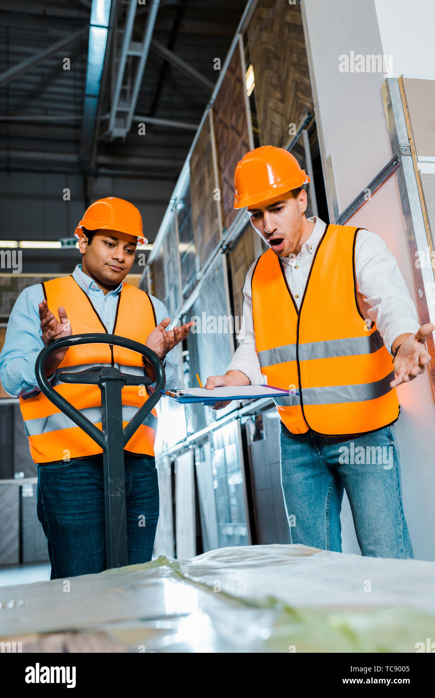 selective focus of angry warehouse worker yelling near indian colleague ...