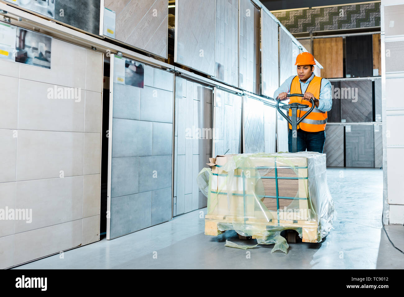 serious indian warehouse worker carrying pallet jack in tiles ...