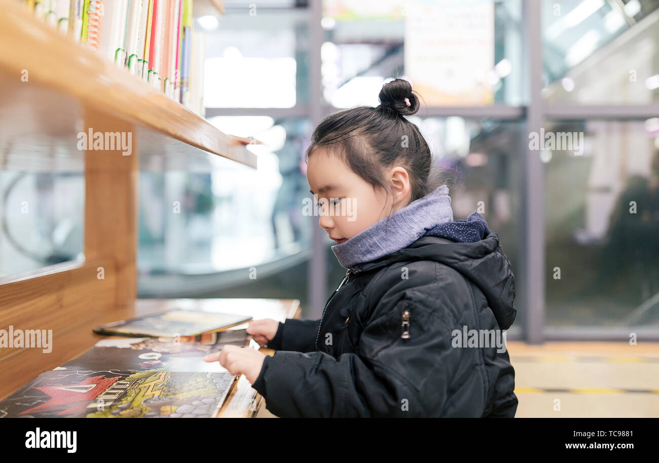 Little Asian girl reading in the library Stock Photo - Alamy