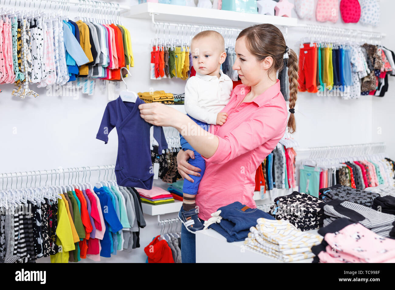 Young happy positive smiling mother is choosing new clothes for her son ...