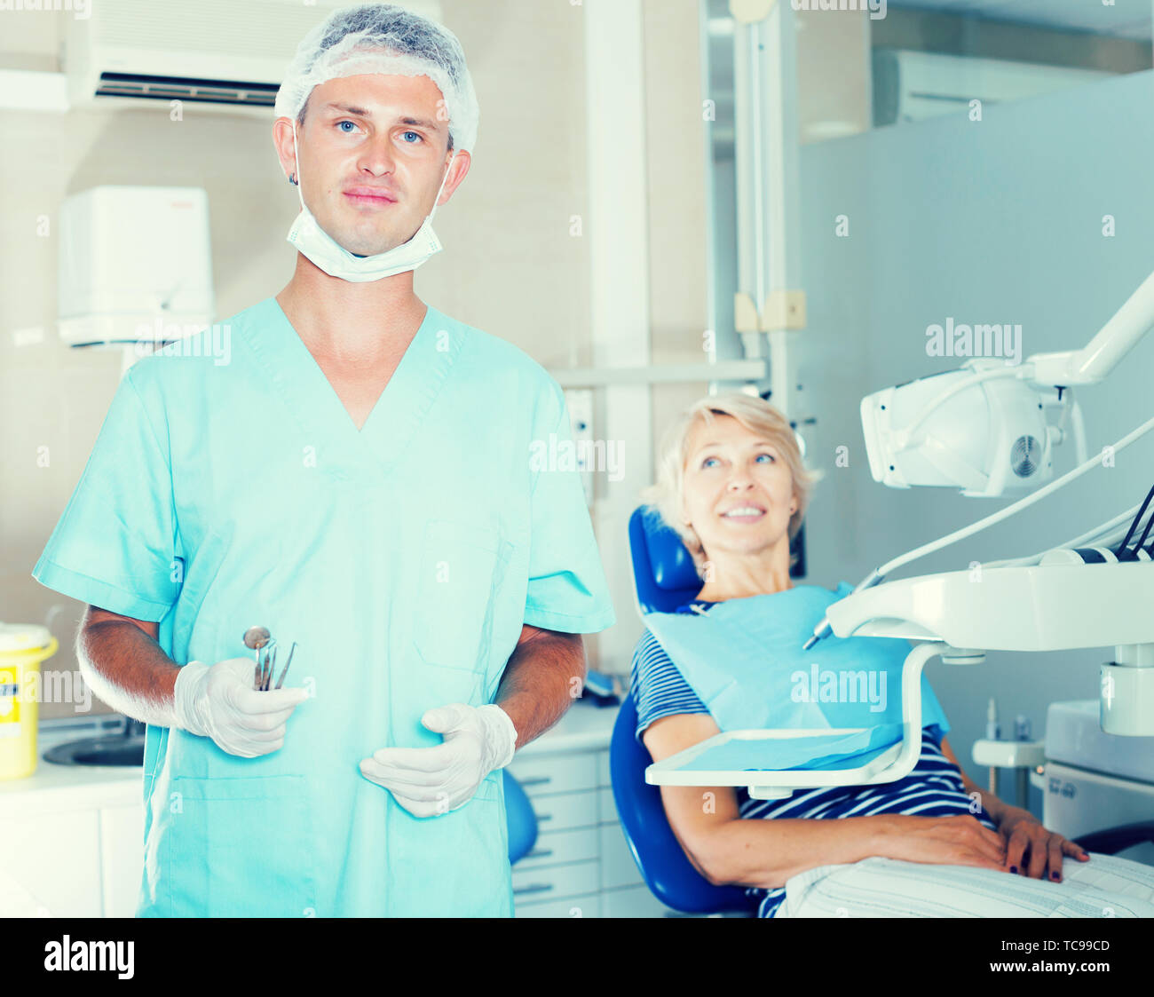 Portrait of professional dentist in dental clinic with patient behind ...