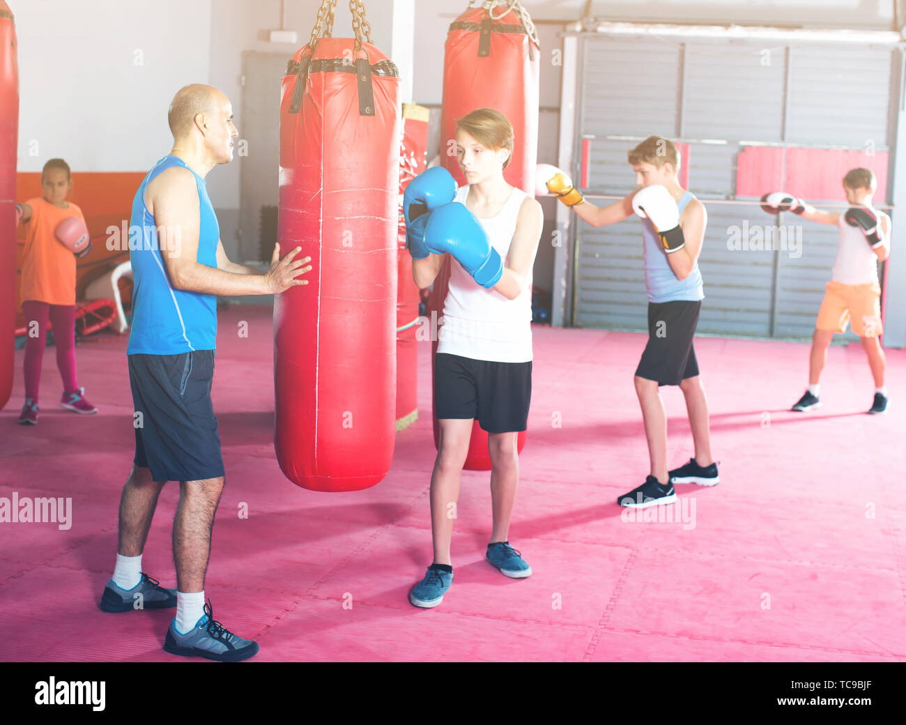 Adult boxing instructor helps children learn techniques of strikes in ...