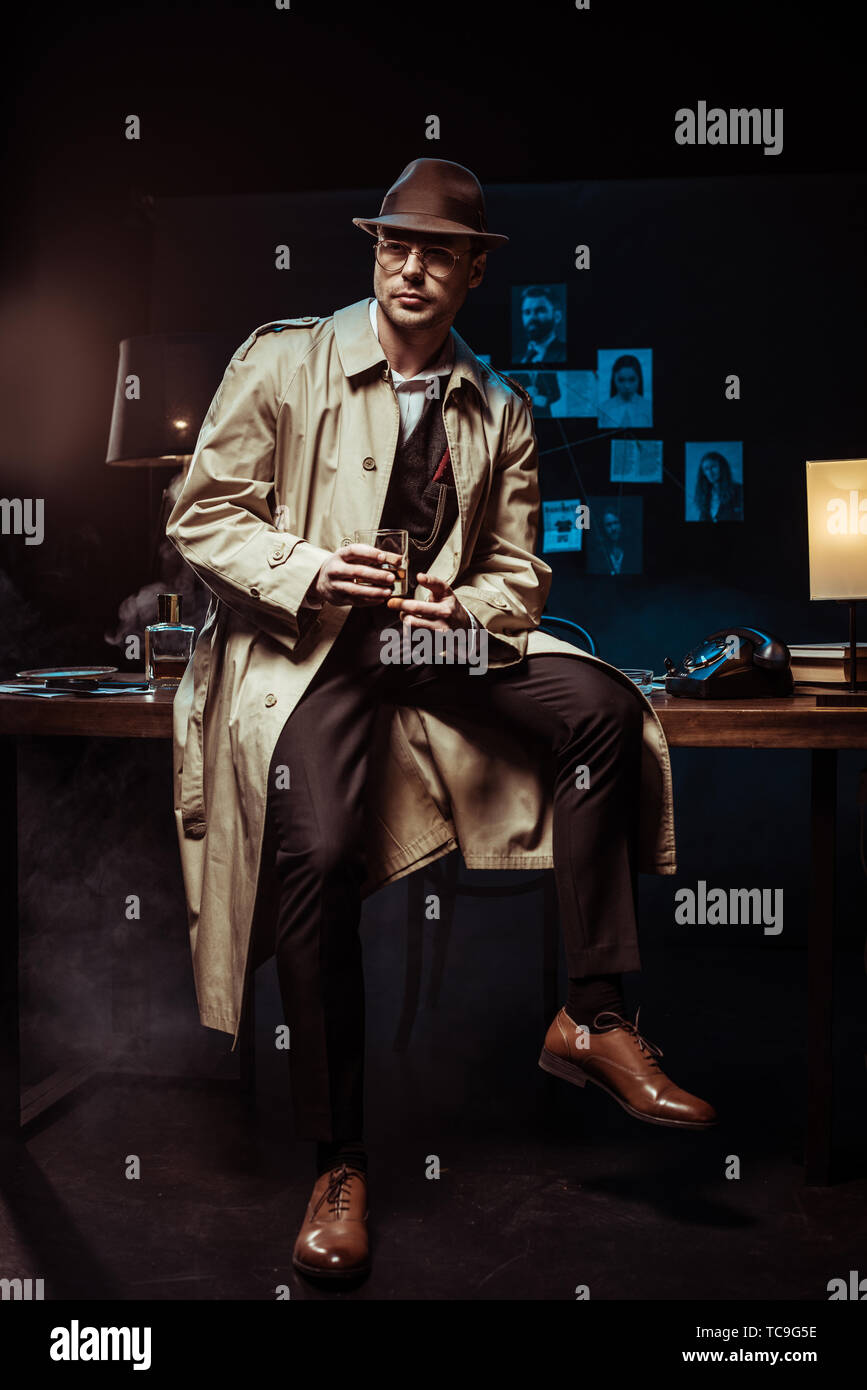 Detective in hat and trench coat sitting on table with glass of cognac ...