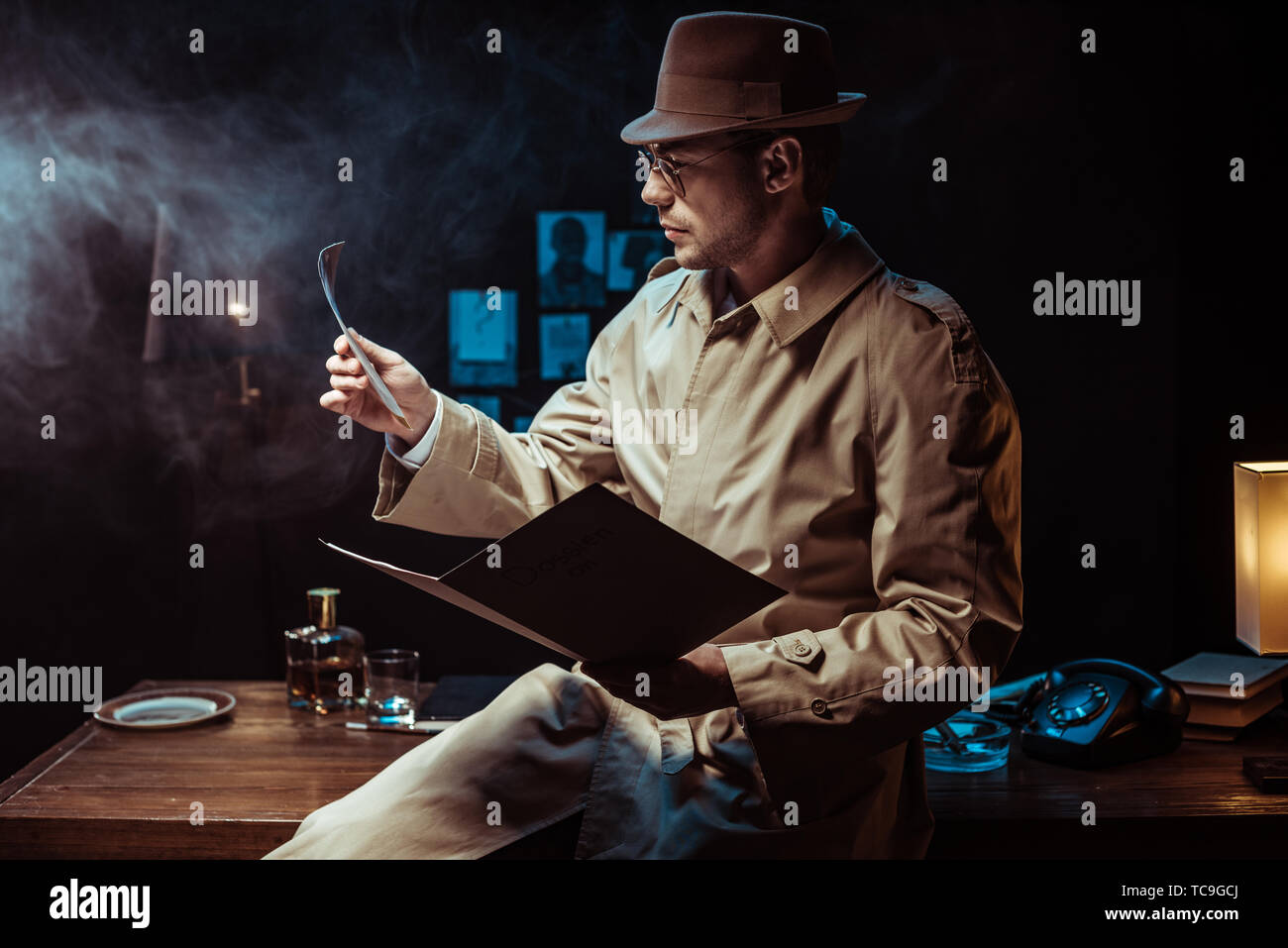 Detective in trench coat and hat holding dossier and looking at photo ...