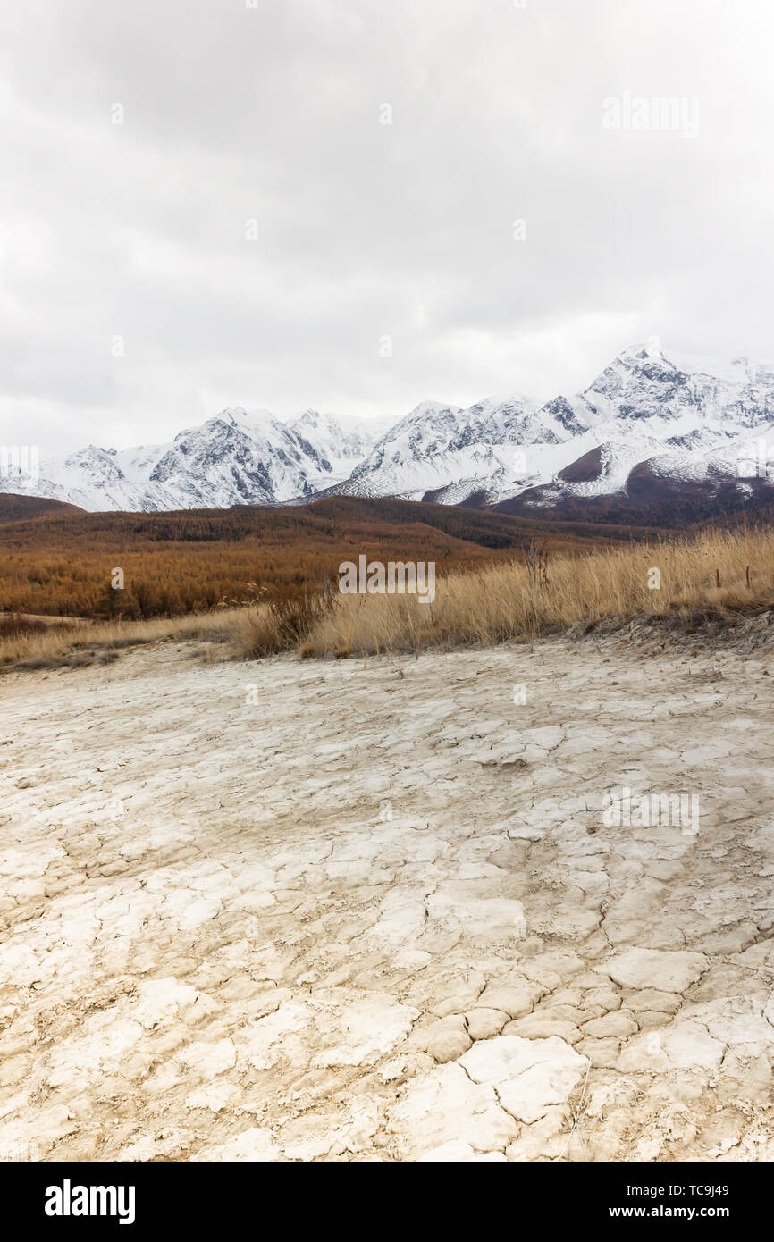 Dry cracked soil in mountain valley. Snowy mountain peaks on horizon ...
