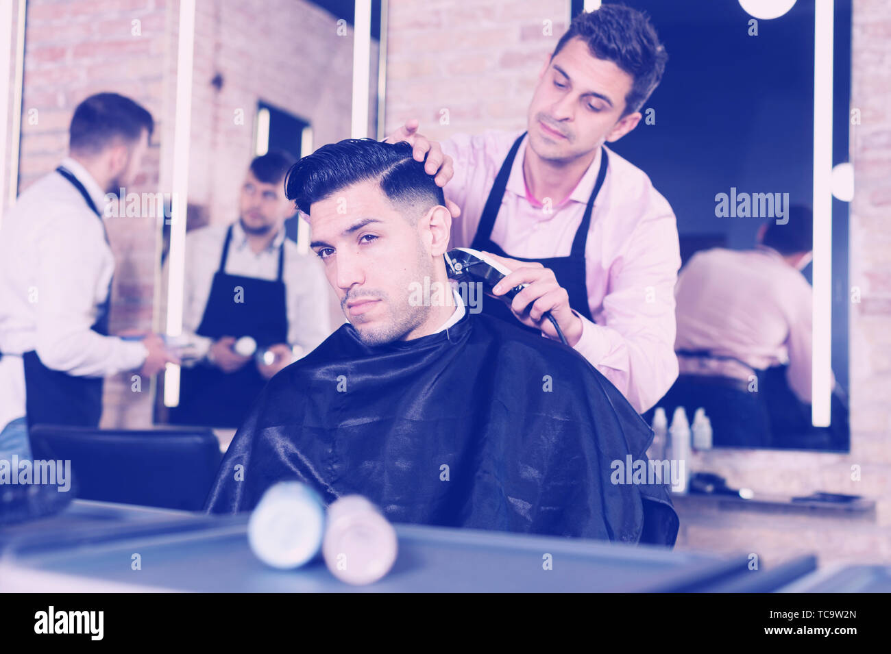 Professional hairdresser man doing styling of handsome guy with ...