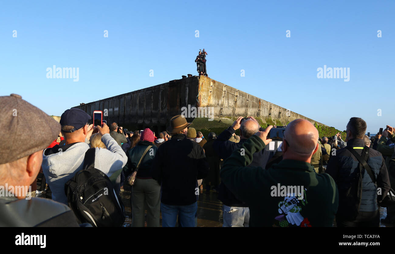 A lone piper plays on the Mulberry harbour at Arromanches in Normandy ...