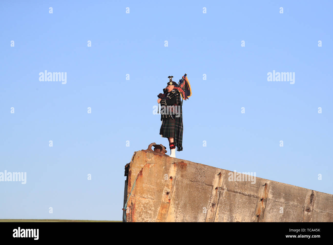 A lone piper plays on the Mulberry harbour at Arromanches in Normandy ...