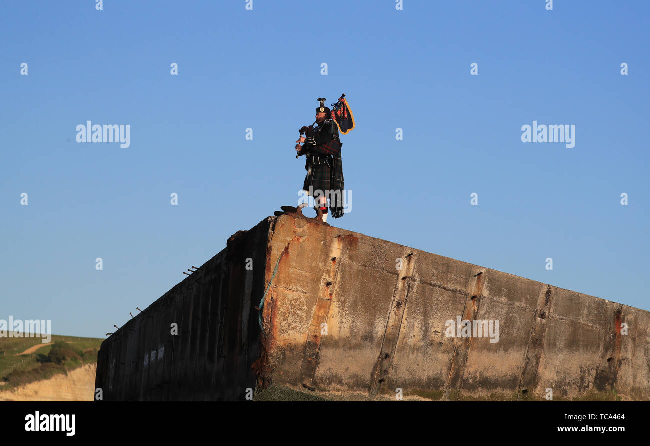 A lone piper plays on the Mulberry harbour at Arromanches in Normandy ...
